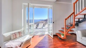 Um interior moderno com piso de madeira, um sofá branco, uma porta de vidro que dá para uma varanda e uma escada de madeira.