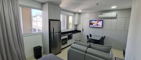 Uma cozinha moderna com geladeira, forno e área de jantar com televisão fixada na parede.