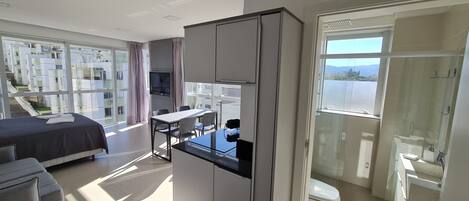 Quarto de hotel moderno com cama, escrivaninha, TV e varanda com vista para a cidade.