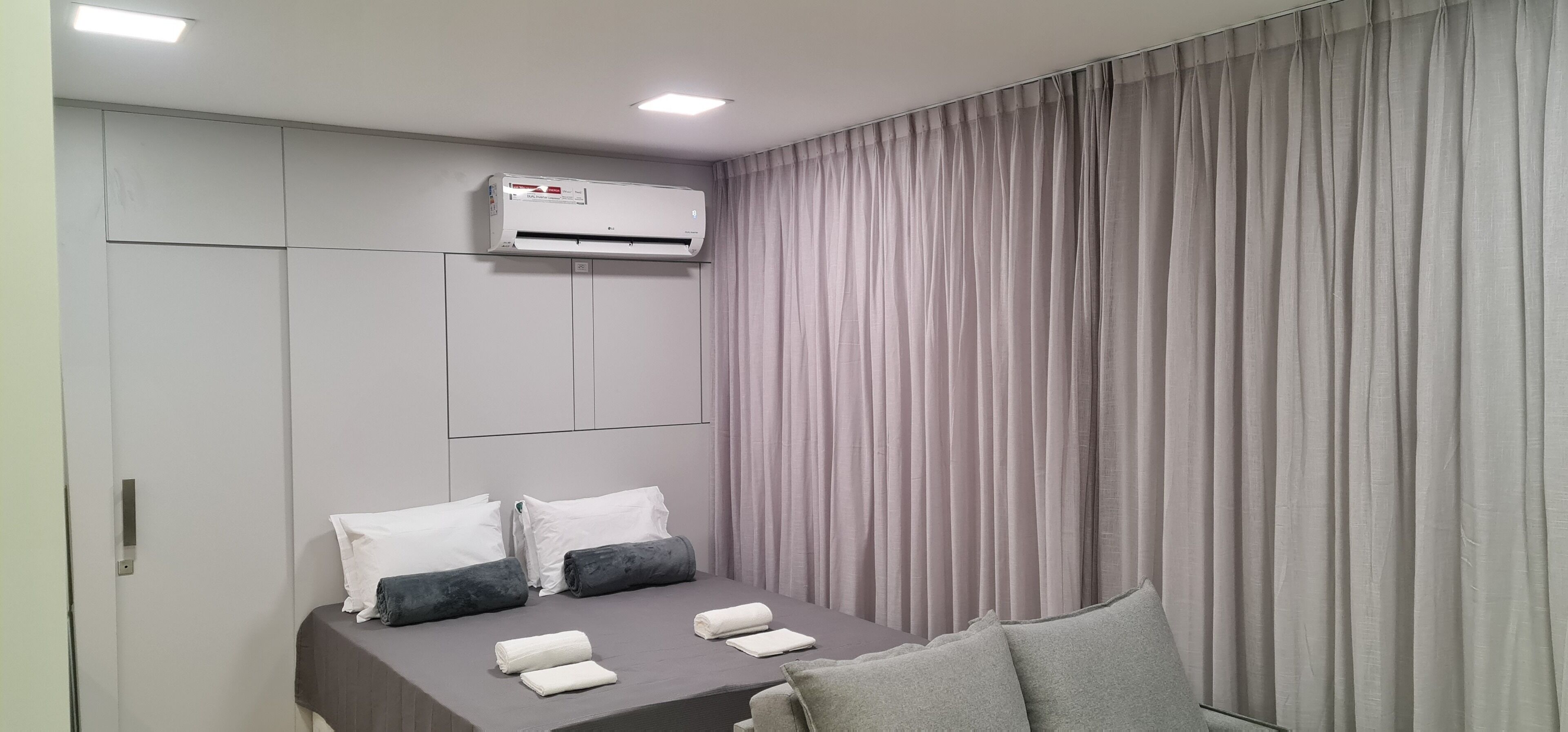 Quarto de hotel com cama, escrivaninha, cadeira, guarda-roupa e ar condicionado.
