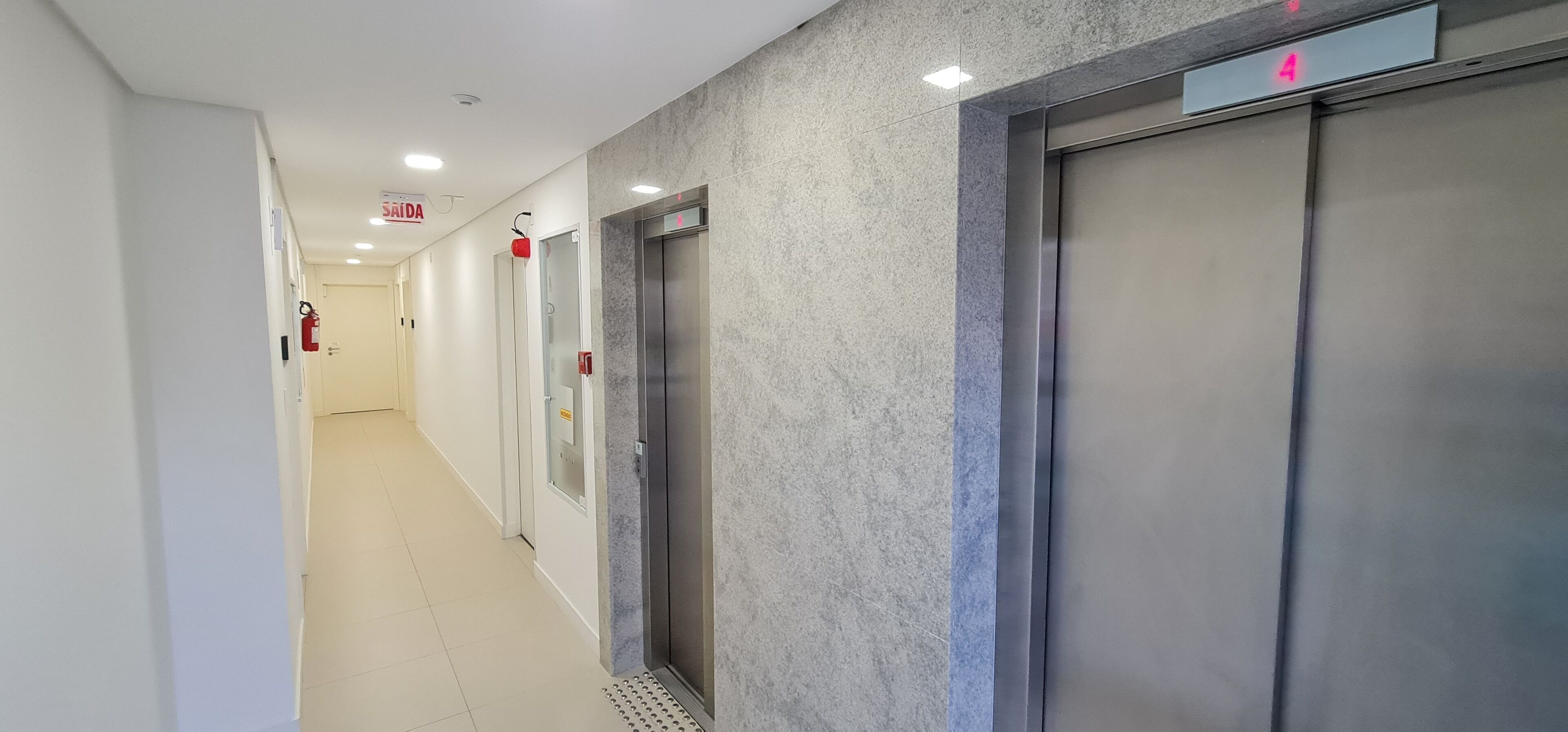 Corredor com dois elevadores, um deles marcado com o número 4, e um extintor de incêndio na parede.
