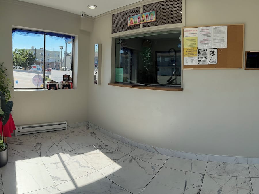 Uma área de recepção de hotel com piso de mármore, uma janela com vista para a rua e diversos avisos afixados.