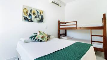 Uma cama de solteiro com um cobertor verde, uma beliche de madeira e um quadro floral na parede.