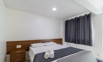 Quarto com cabeceira de madeira, cama com roupa de cama branca e um cobertor cinza, além de uma toalha enrolada.