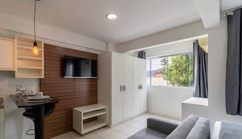 Uma sala de estar moderna com televisão de tela plana, uma área de jantar com mesa posta para dois e uma grande janela com vista.