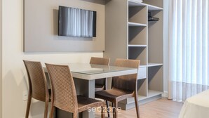 Uma sala de jantar moderna com mesa de vidro e cadeiras de vime, televisão integrada e um aparador com espaço de armazenamento.