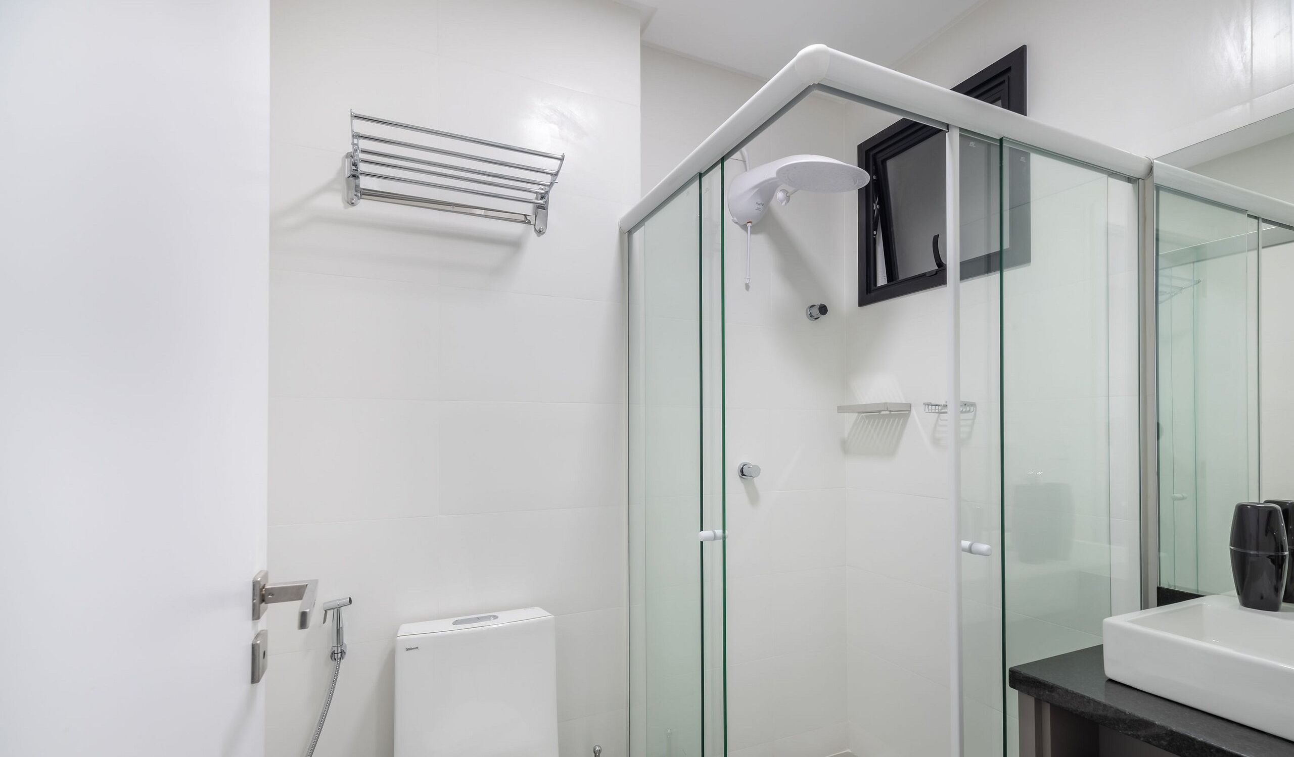 Um banheiro moderno com box de vidro, pia branca e porta-toalhas.