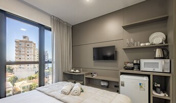 Quarto de hotel com cama, televisão, cafeteira, micro-ondas e vista da cidade.