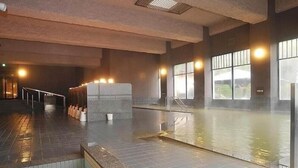 Uma grande piscina interior com piso de azulejos, um banco de pedra e uma escadaria que leva a um andar superior.