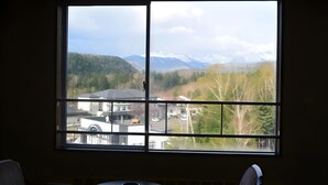 Quarto com uma grande janela que oferece vista para uma floresta, montanhas e edifícios.