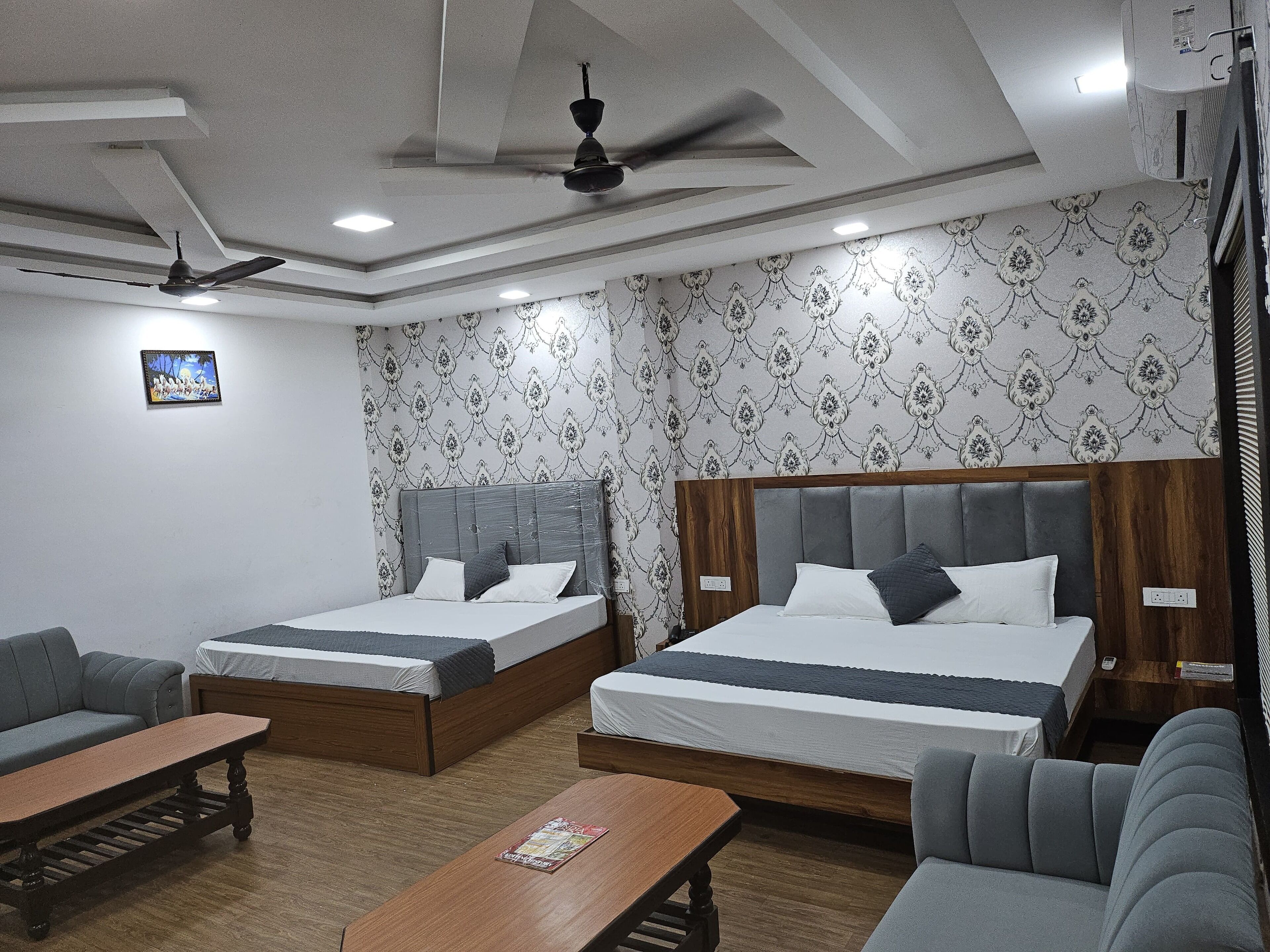 Quarto de hotel com duas camas, um sofá, uma mesa de centro e um ventilador de teto.