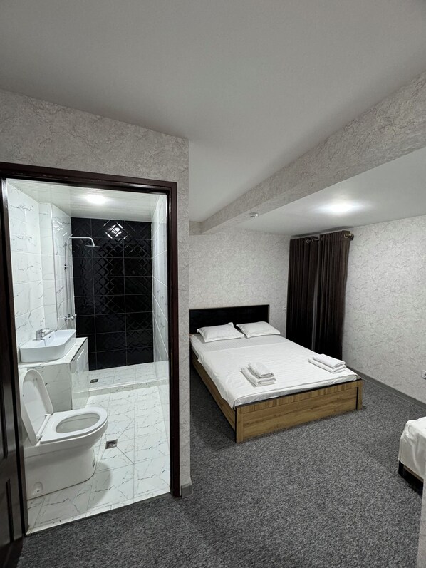 Quarto de hotel com uma cama, banheiro com chuveiro e vaso sanitário.