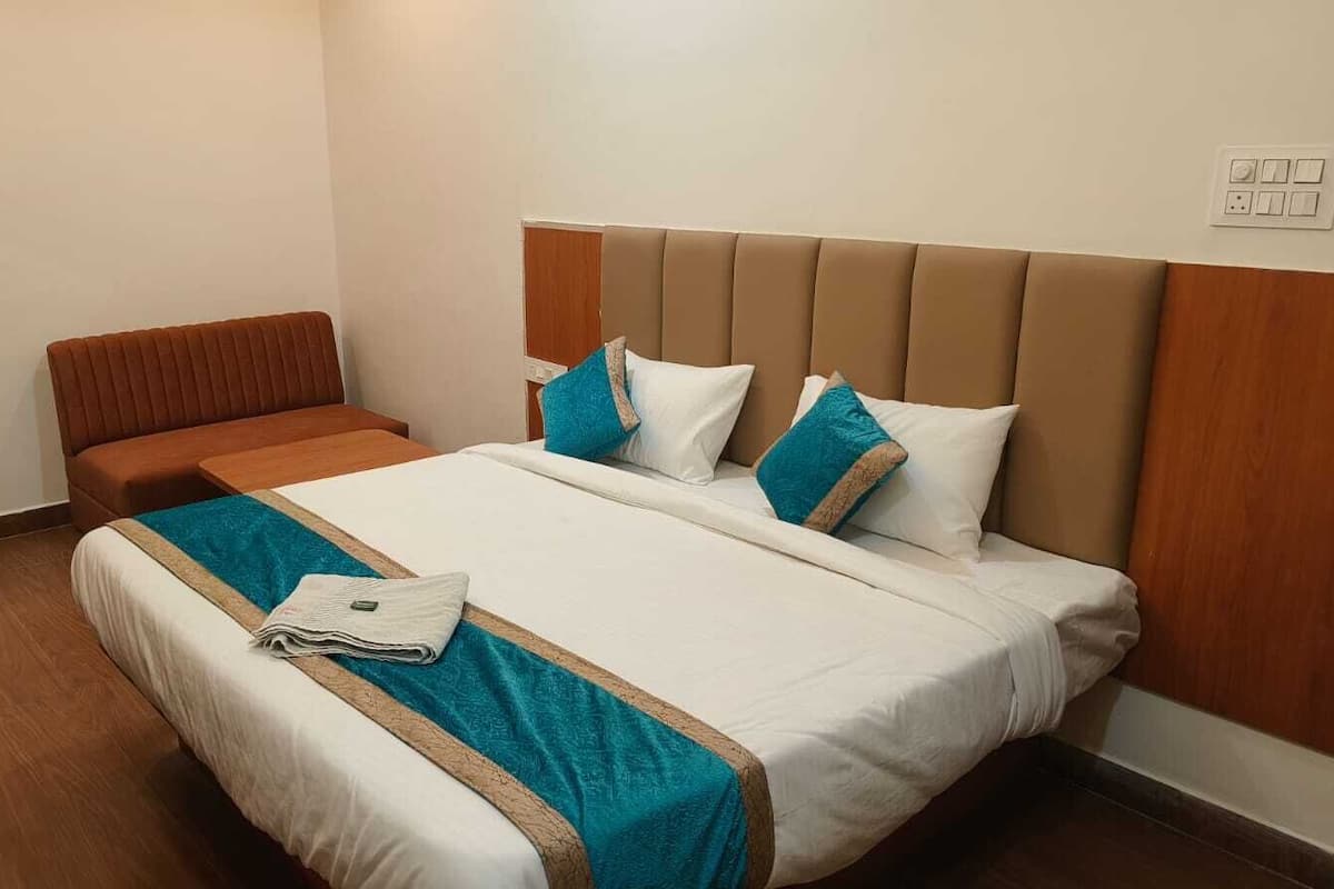 Quarto de hotel com cama, um banquinho e cabeceira de madeira.