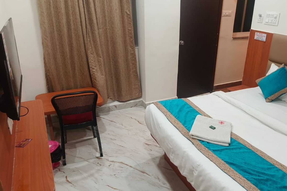 Quarto de hotel com cama, escrivaninha, cadeira e televisão.