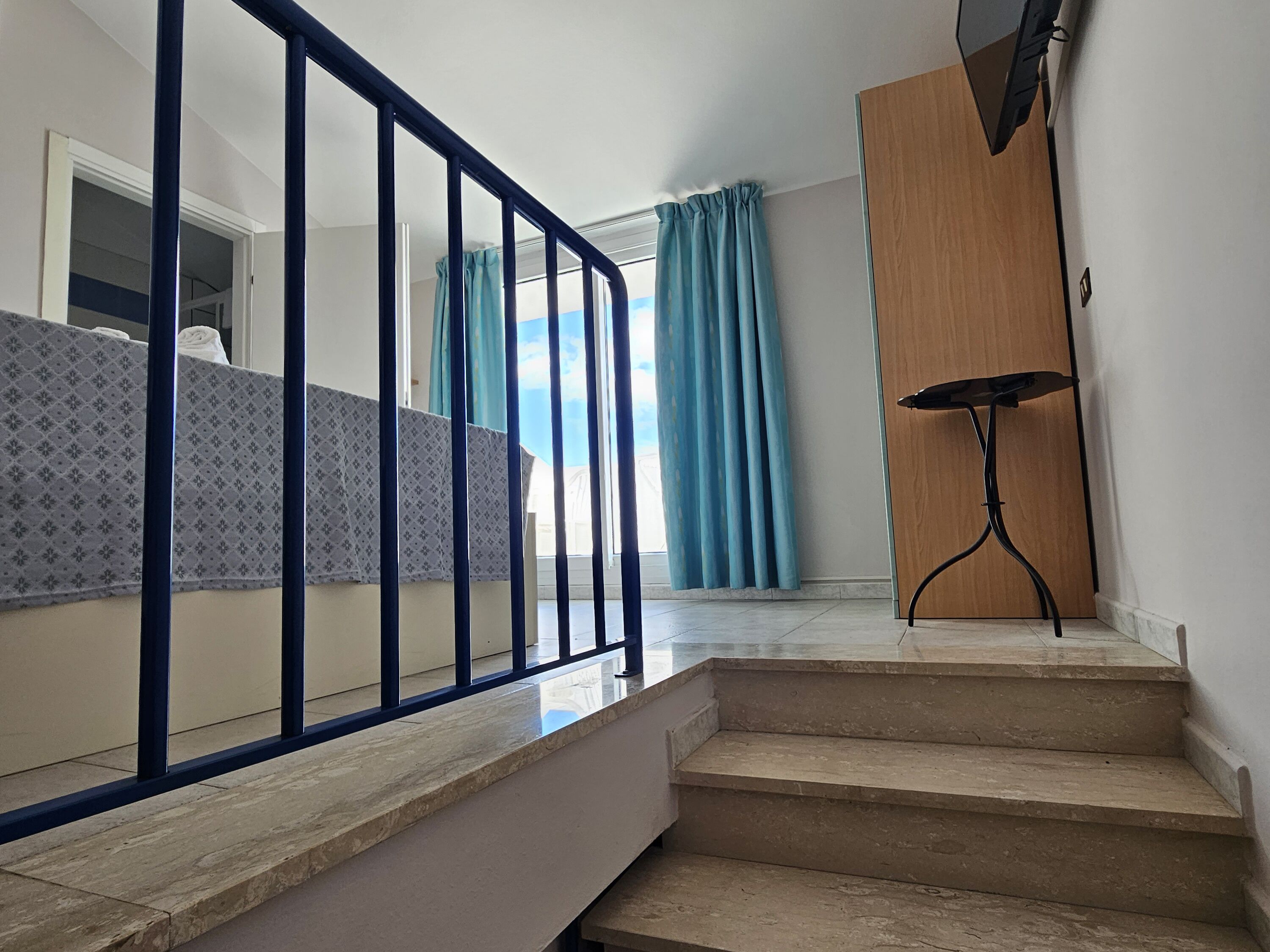 Escada que leva a um quarto com uma cama, uma porta de madeira e uma pequena mesa.
