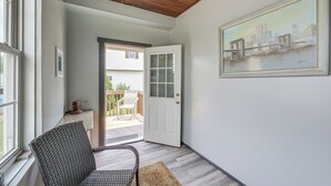 Quarto com teto de madeira, porta branca, cadeira de vime e um quadro na parede.