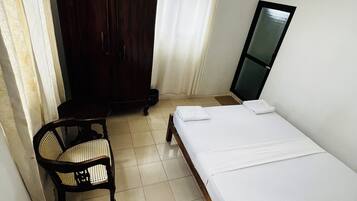 Quarto pequeno e limpo com uma cama de solteiro, um guarda-roupa de madeira, uma cadeira e um espelho na parede.