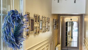 Um corredor com luminária moderna, fileira de quadros e planta decorativa azul.