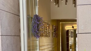 Corredor com porta de vidro, espelho fixado na parede e planta decorativa.