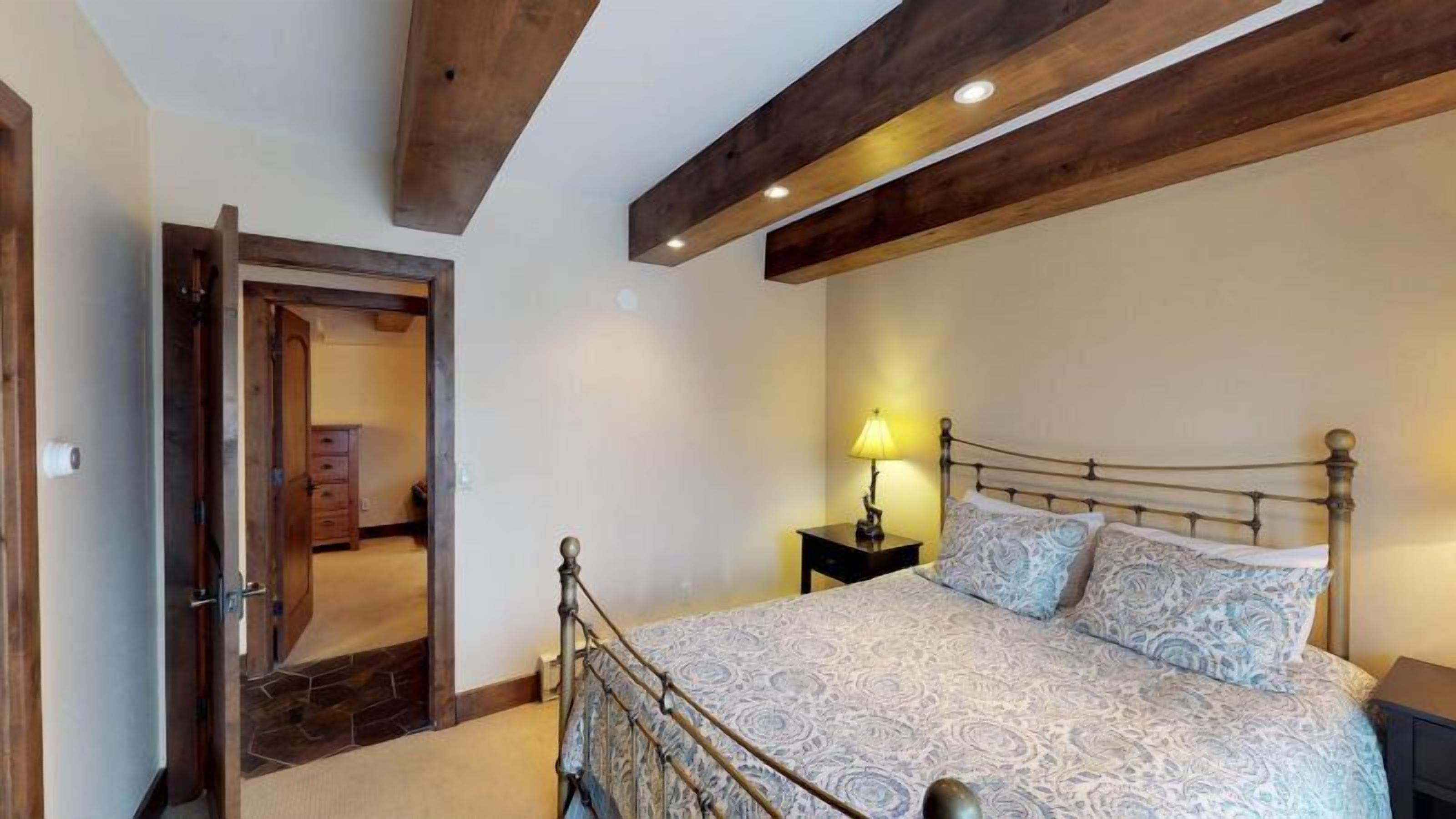 Quarto com cama, mesa de cabeceira, abajur e teto de madeira.