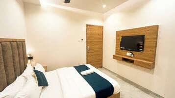 Quarto de hotel moderno com uma cama, um ventilador de teto, uma TV fixada na parede e uma porta de madeira.