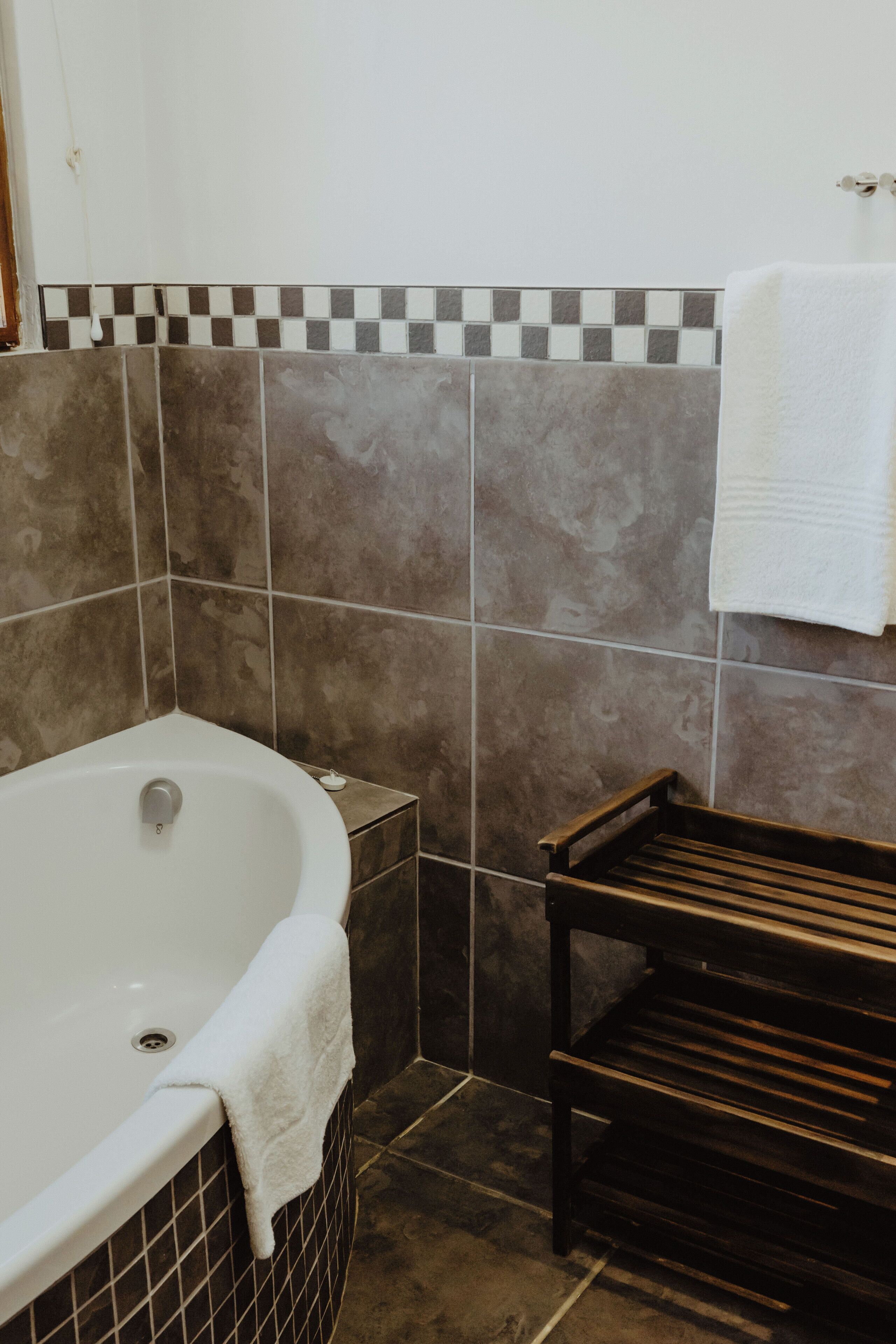 Um banheiro com banheira, um banco de madeira e uma parede revestida de azulejos.
