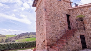 Um edifício de pedra com uma pequena janela e uma porta, cercado por um viveiro e com vista para campos verdes.