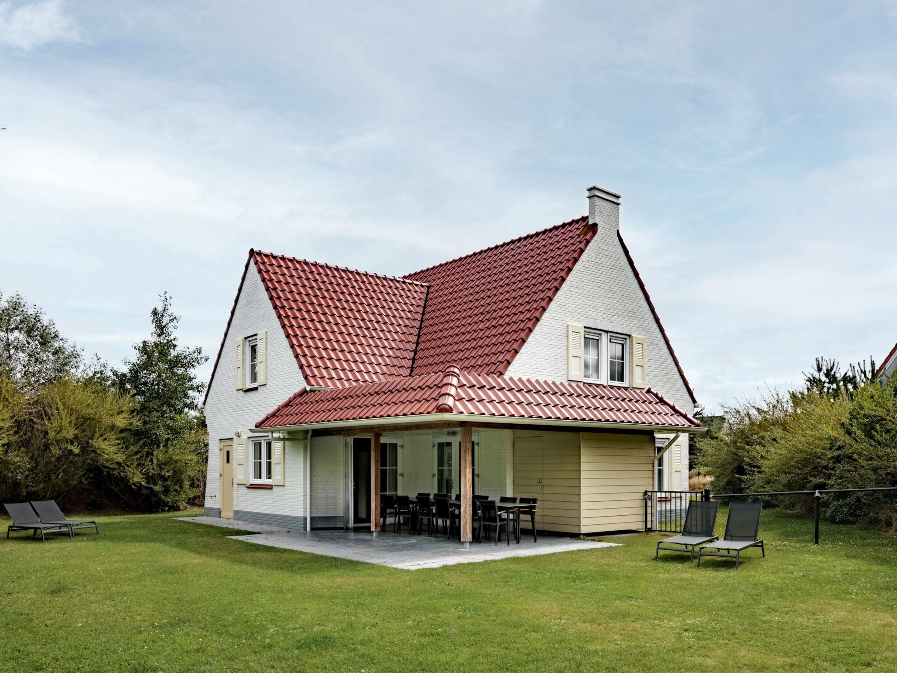 Uma casa com telhado vermelho inclinado, varanda coberta com área de estar ao ar livre e gramado bem cuidado.