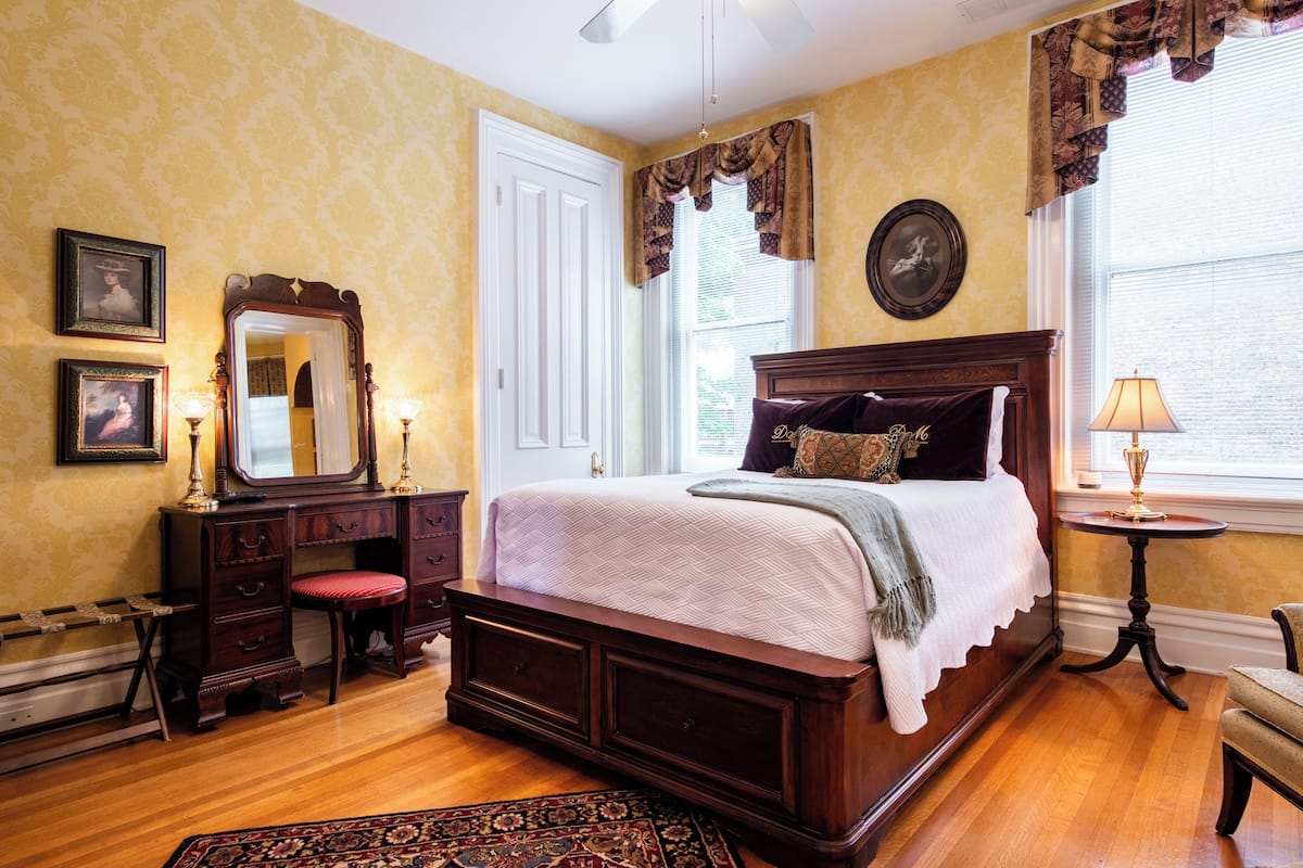 Quarto com uma cama grande, cômoda, espelho e janela com cortinas.
