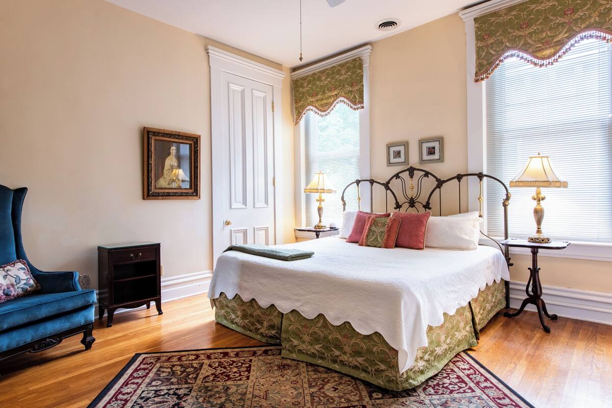 Quarto com cama grande, penteadeira, cadeira e duas mesas de cabeceira com abajures.