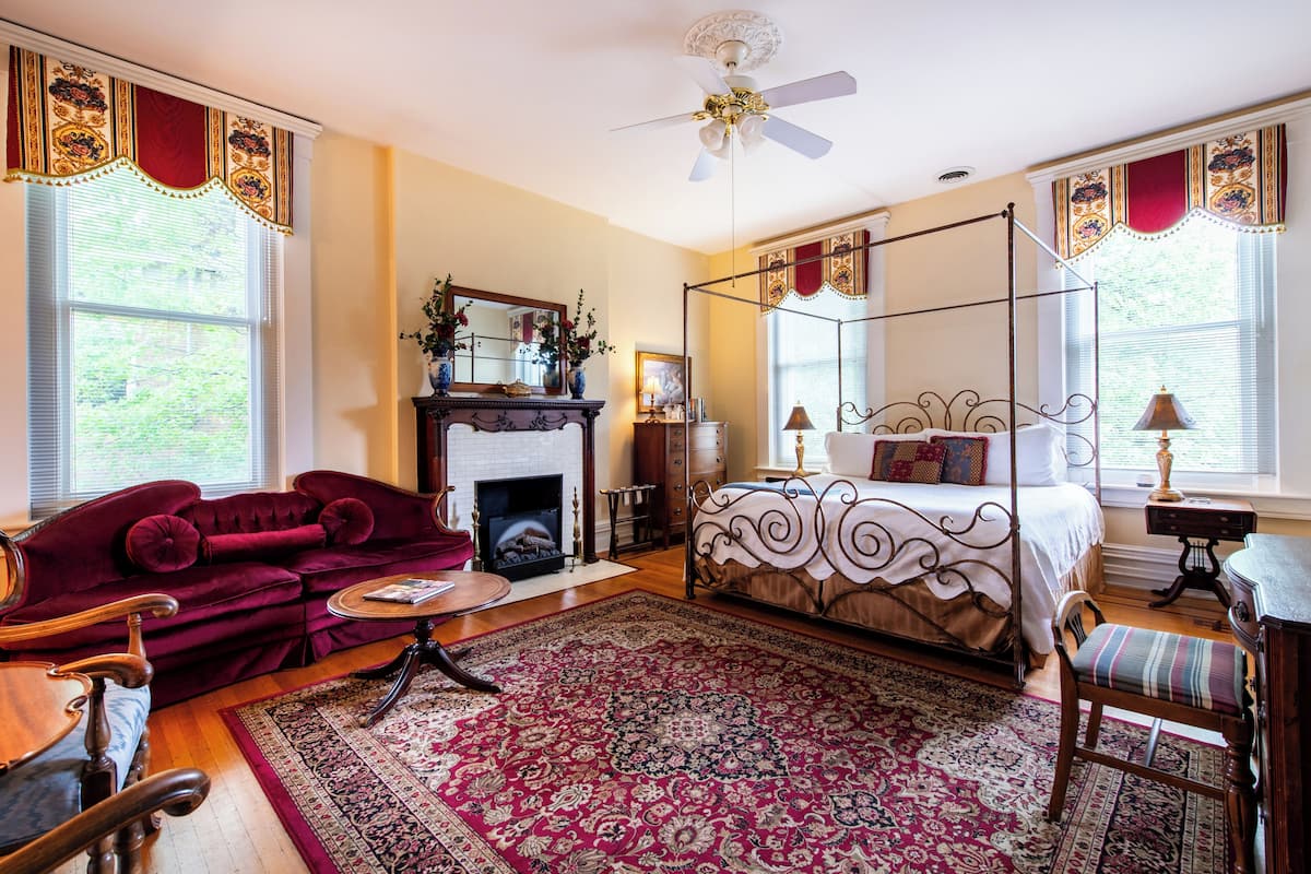 Quarto com uma cama de dossel, lareira, sofá de veludo vermelho e um tapete grande e ricamente decorado.