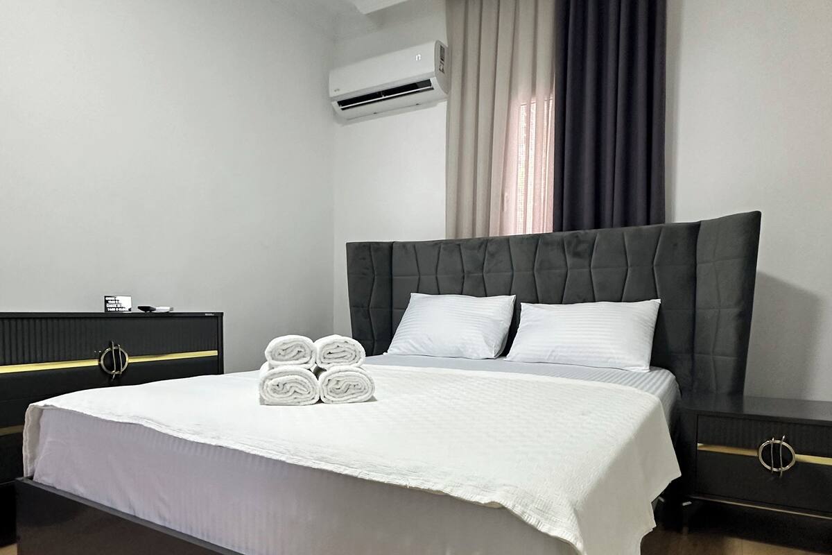 Quarto de hotel moderno com uma cama grande, mesa de cabeceira, guarda-roupa e ar condicionado.