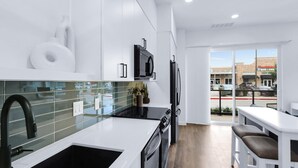 Uma cozinha moderna com armários brancos, uma pia preta e uma janela grande com vista para a rua.