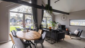 Uma sala de estar moderna com uma mesa de jantar de madeira, cadeiras estofadas cinzas, um sofá e uma TV.