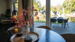 Uma mesa de jantar com um vaso de flores, um tabuleiro e vista para um pátio com mobiliário exterior.