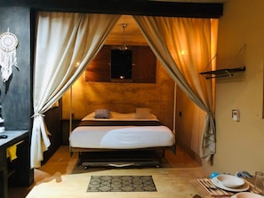 Um quarto aconchegante com cama, cortinas, um adorno de penas e uma mesinha de cabeceira.