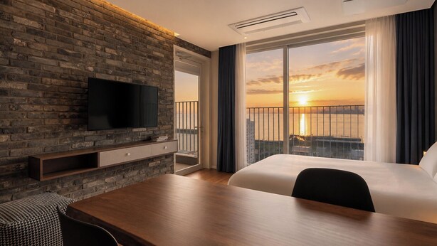 Quarto de hotel com parede de tijolos, televisão de tela plana, escrivaninha de madeira, cama e varanda com vista para o pôr do sol.