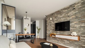 Uma sala de estar moderna com parede de tijolos, uma TV de tela plana, um sofá, uma mesa de centro e uma área de jantar com um vaso de flores.