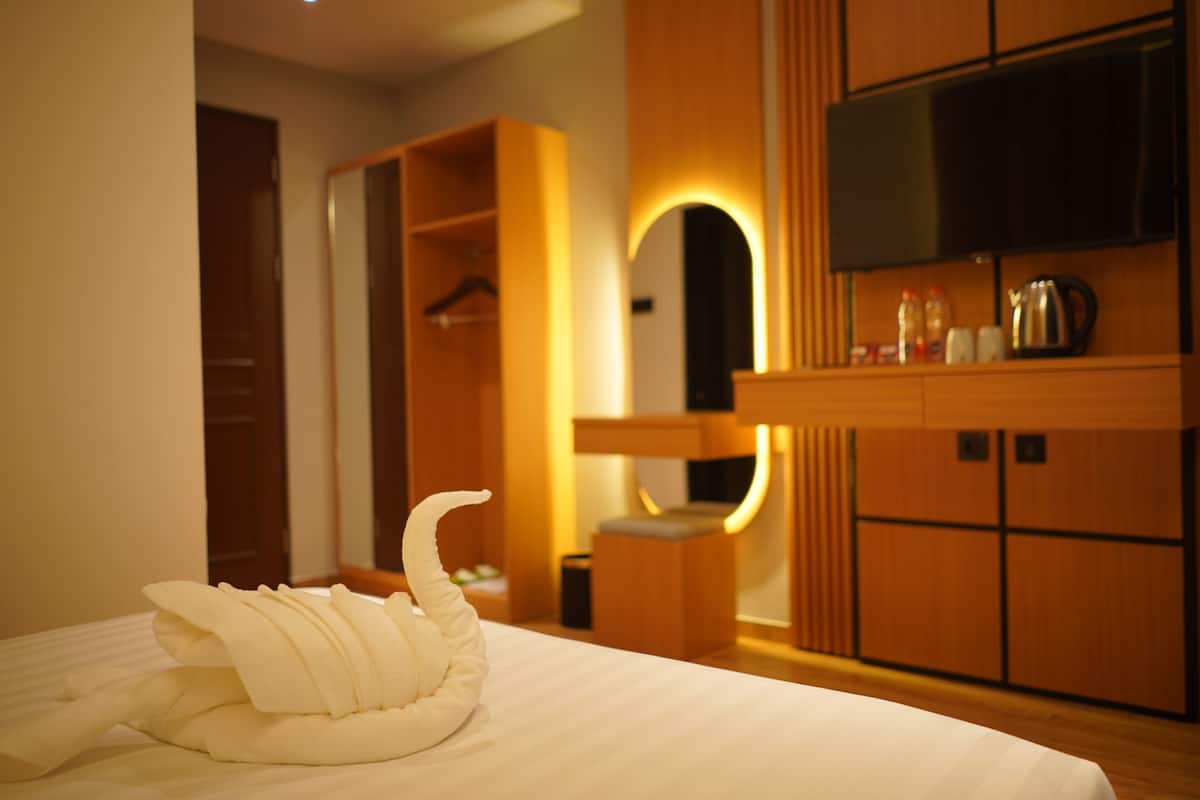 Quarto de hotel com cama arrumada, televisão fixada na parede e guarda-roupa de madeira com espelho.