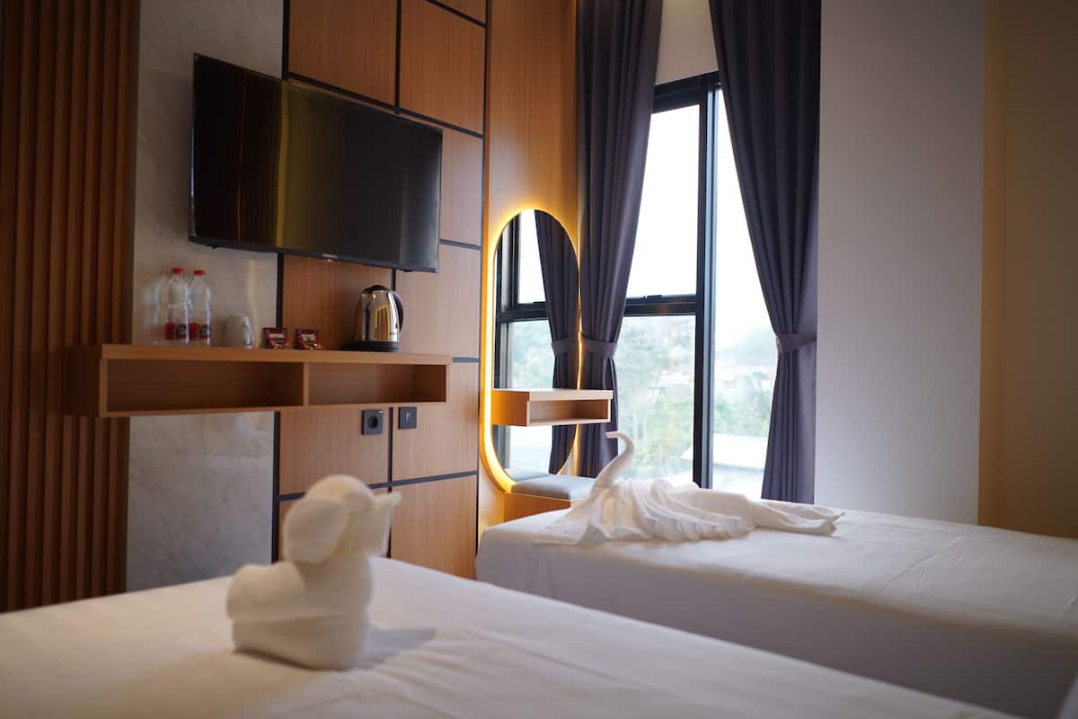 Quarto de hotel com duas camas, televisão fixada na parede, espelho e janela com cortinas.