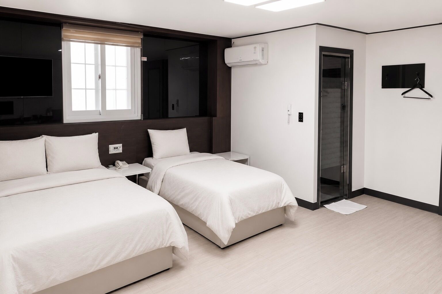 Quarto de hotel com duas camas, televisão, janela com persianas, ar condicionado e porta de acesso a um banheiro.