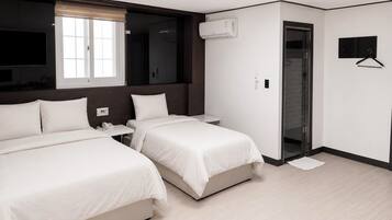 Quarto de hotel com duas camas, televisão, janela com persianas, ar condicionado e porta de acesso a um banheiro.