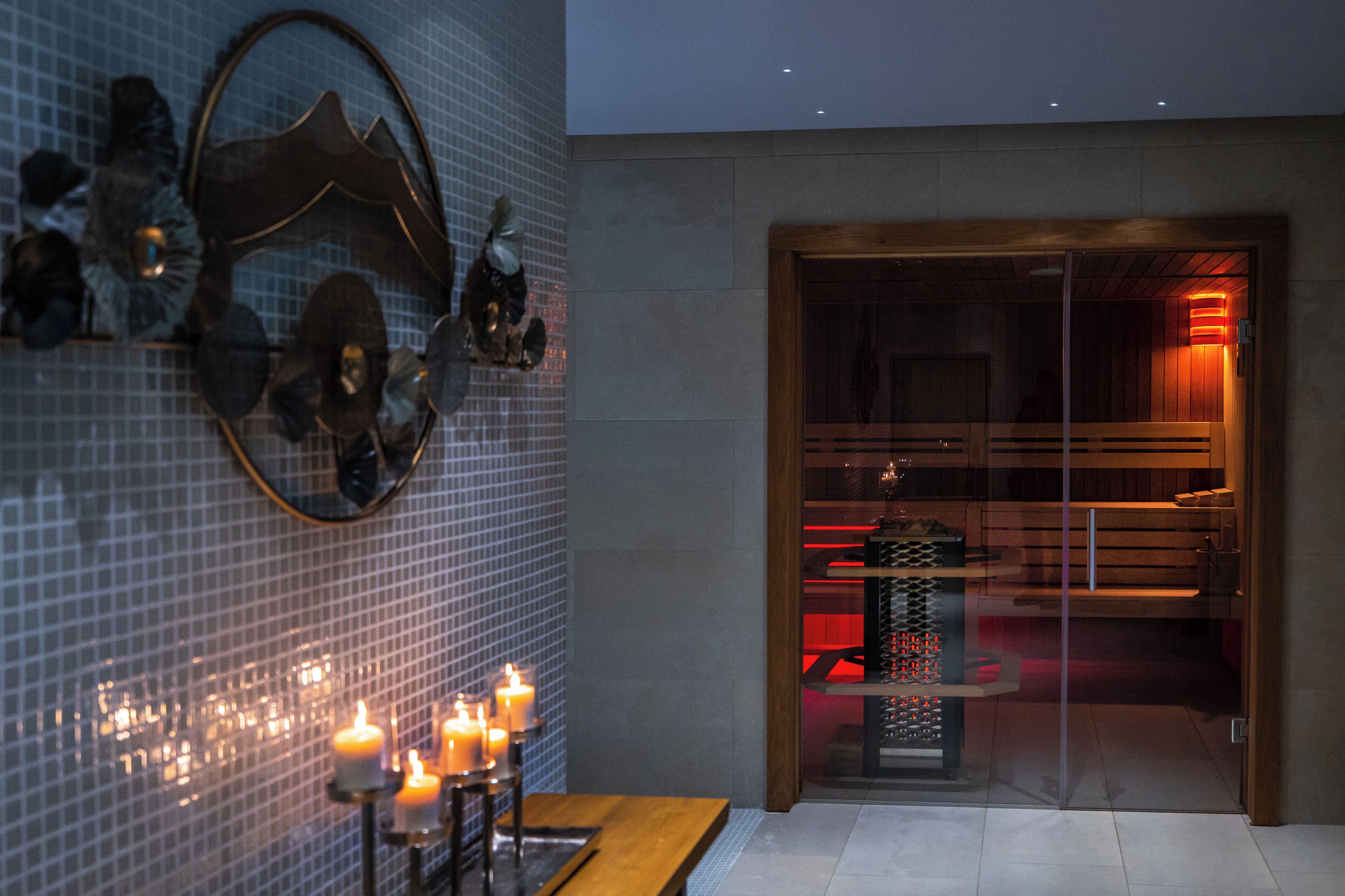 Um interior moderno com parede azulejada, um banco de madeira e uma porta de vidro que dá para um espaço com uma estante iluminada em vermelho.