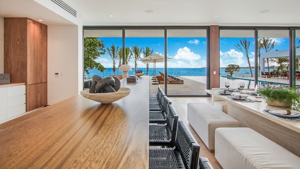 Uma sala de jantar moderna com uma mesa de madeira, cadeiras pretas e vista para o oceano.
