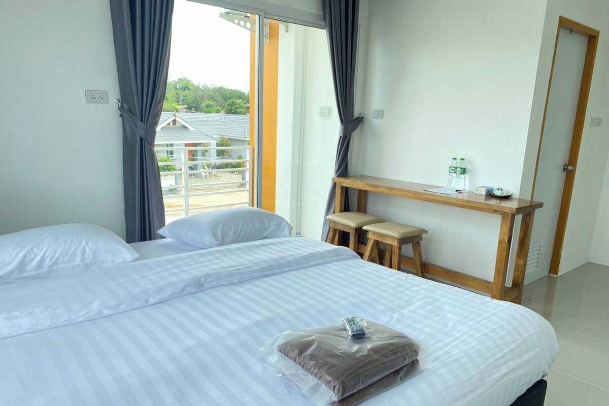 Quarto de hotel com uma cama grande, uma escrivaninha de madeira e vista para o exterior.