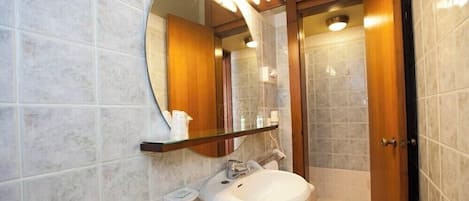 Uma casa de banho com uma pia branca, um espelho e uma zona de duche.