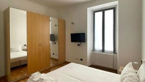 Quarto com uma cama grande, um guarda-roupa, uma televisão e uma janela.
