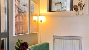 Um quarto com um sofá verde, uma mesinha com um vaso e duas luminárias fixadas na parede.