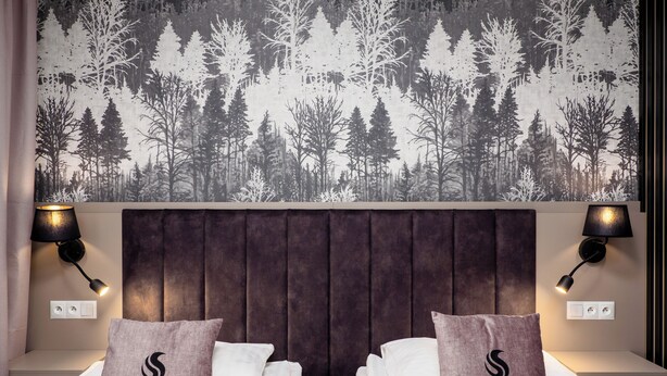 Quarto de hotel com duas camas, cabeceira escura e papel de parede com tema de floresta.
