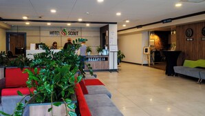 Uma área de recepção de hotel com balcão, sala de espera com assentos vermelhos e cinzas, e uma parede com relógio e uma placa que diz "New York".